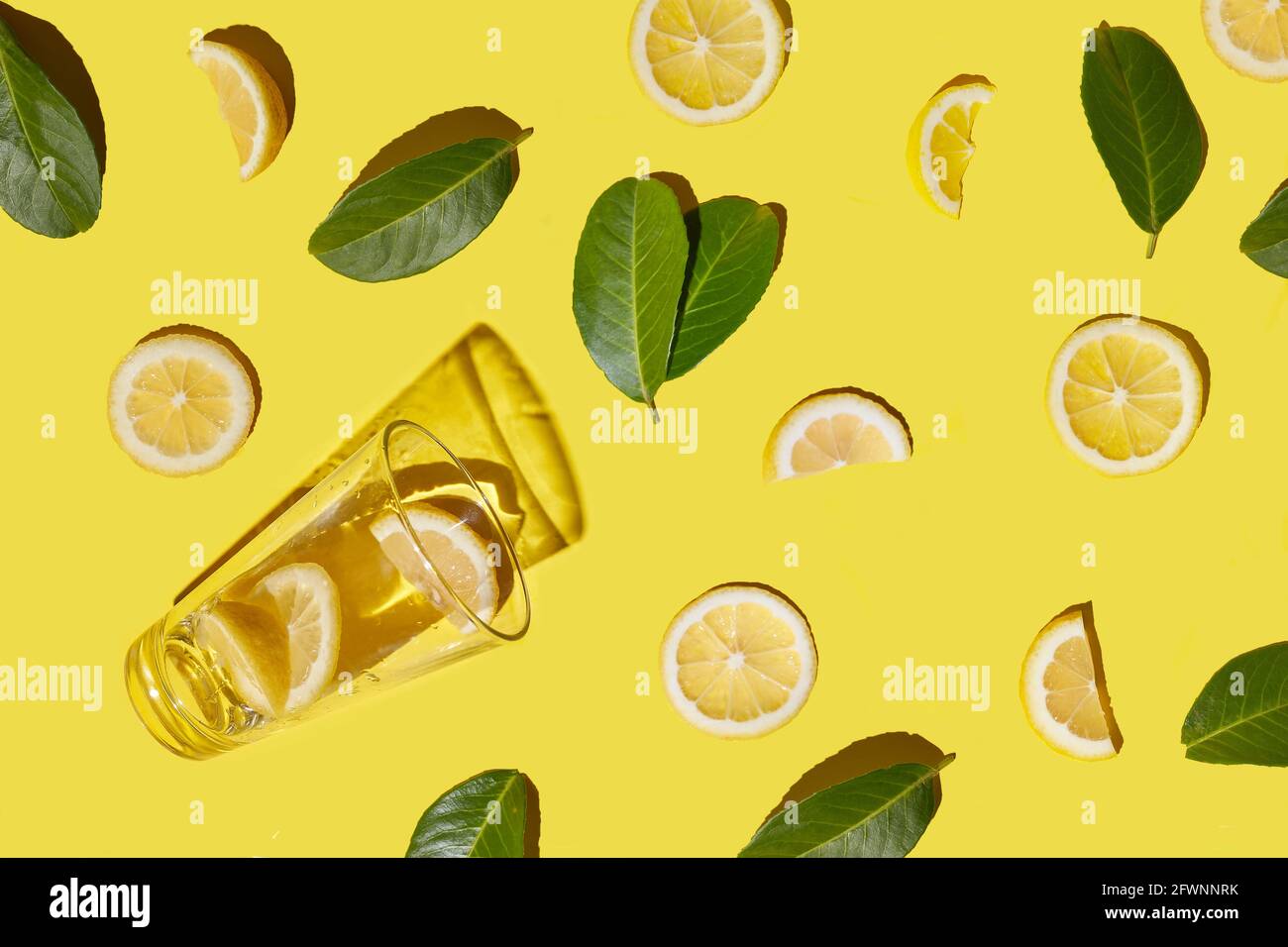 Flat lay Lemonade in glass with lemons and green leaves on yellow paper ...