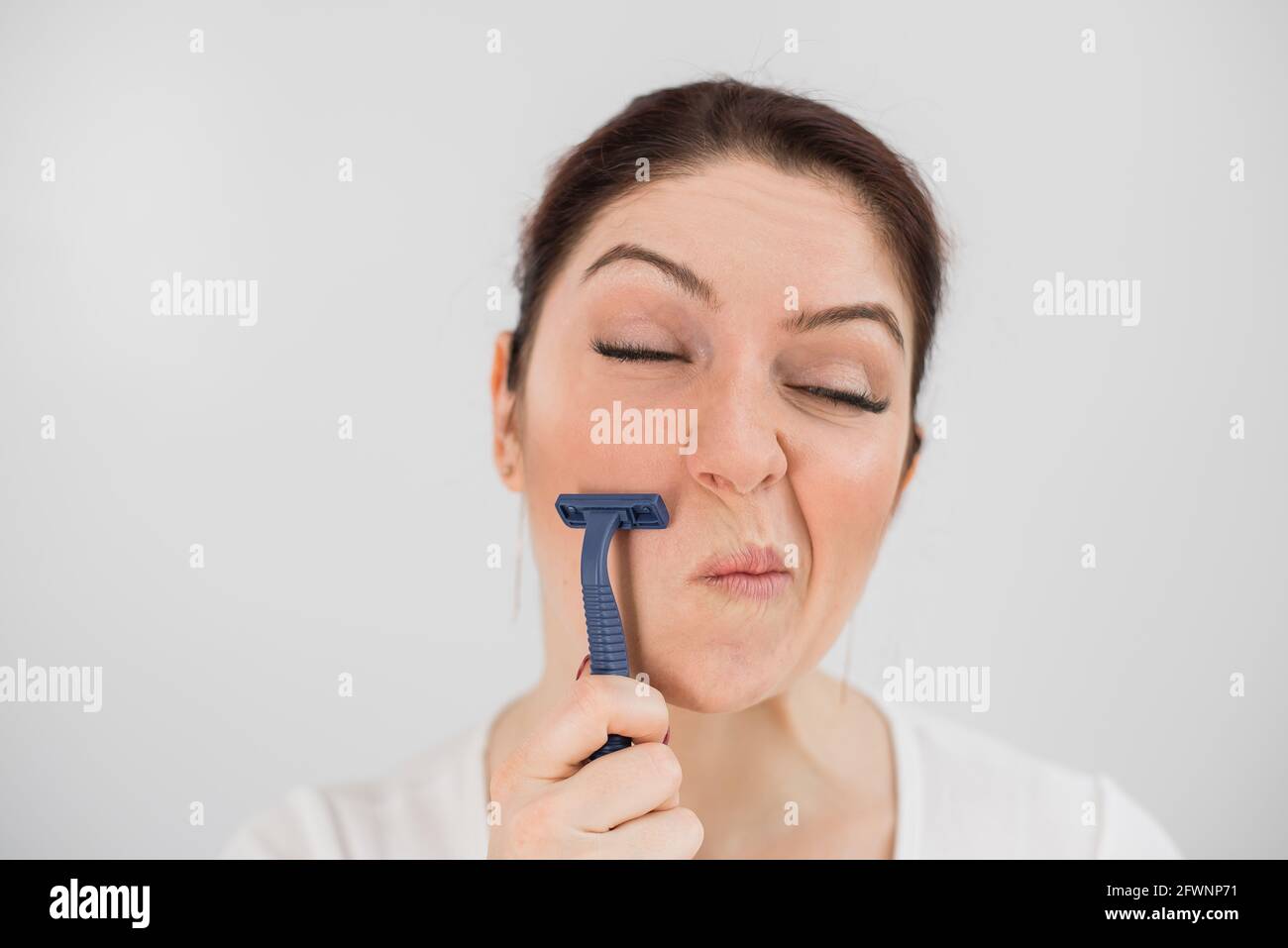 Caucasian funny woman shaves her face with a straight razor on a white ...