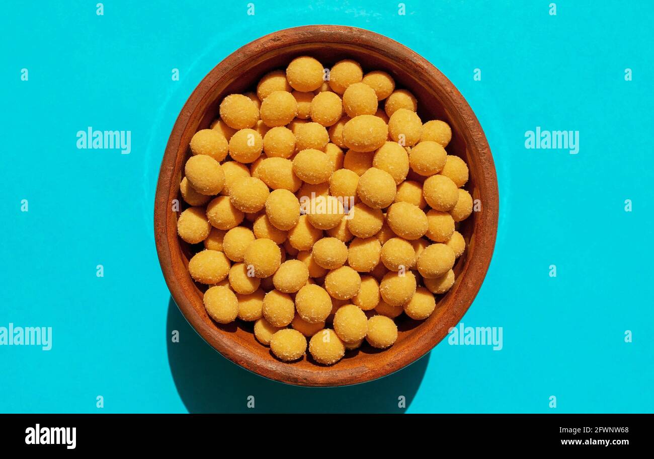 Cheese-coated salted peanuts in a brown bowl on blue background. Fried ...