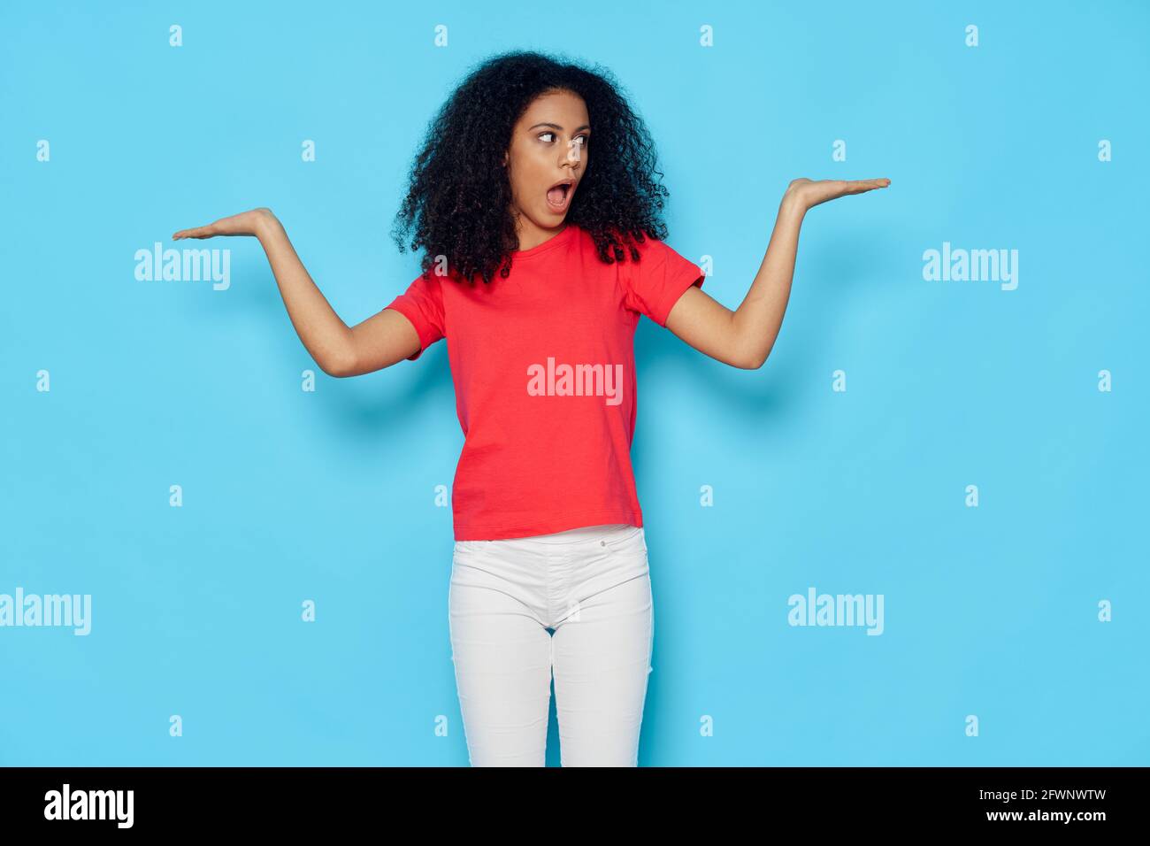 woman with curly hair shrug to the sides on a blue background and ...