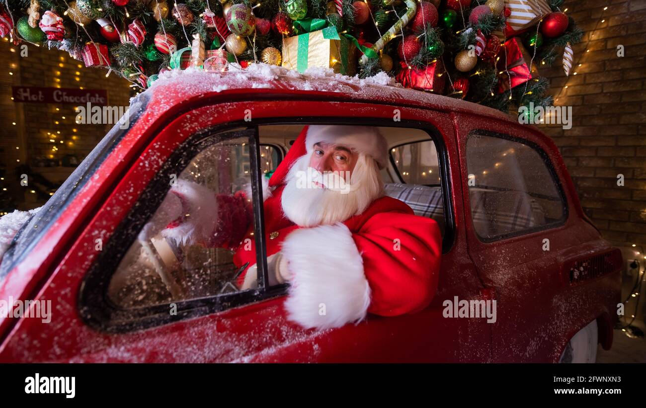 Portrait of santa claus driving a car loaded with a Christmas tree and ...