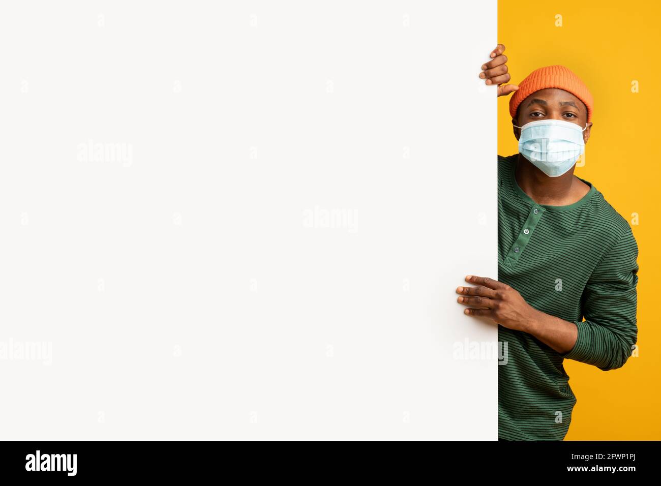 Black young man in medical mask standing behind blank white ...