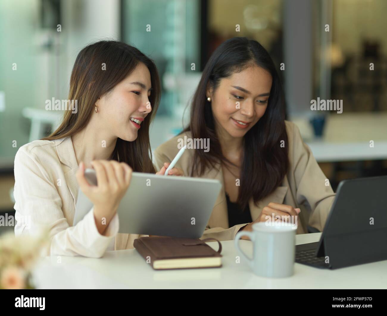 Portraits of two businesswomen talking to each other while working in ...