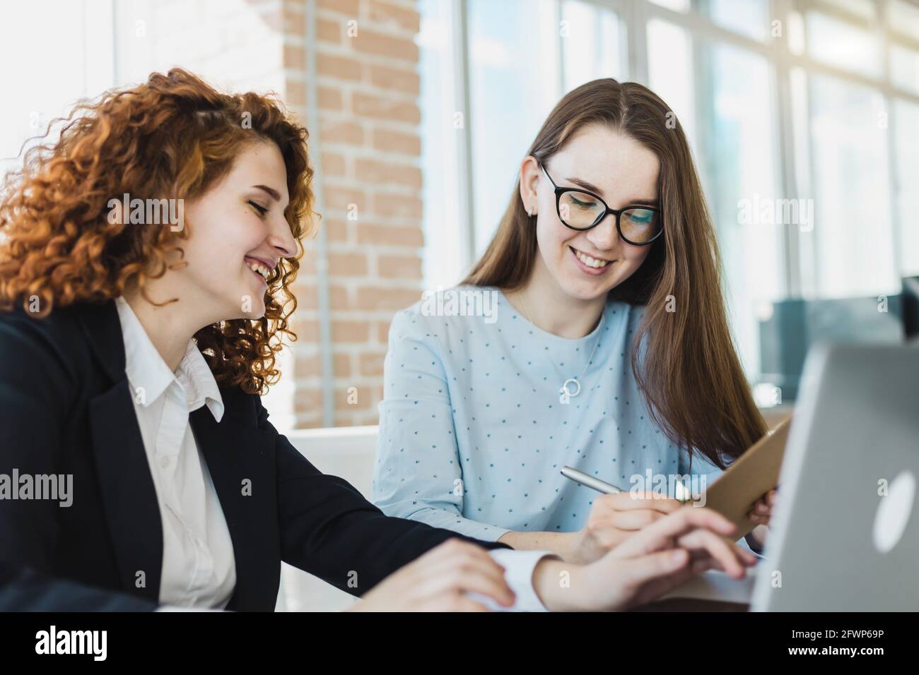 Two beautiful young woman talking and discussing working moments with ...