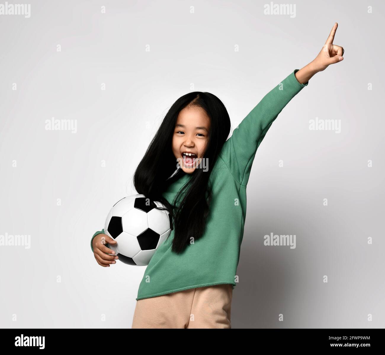 Happy screaming Asian kid girl holding soccer football ball in one hand ...