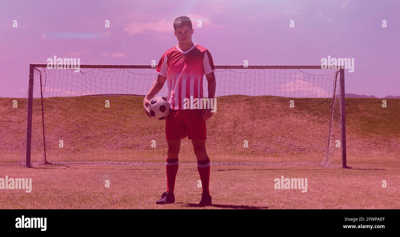 Composition of footballer holding ball on football pitch with pink ...