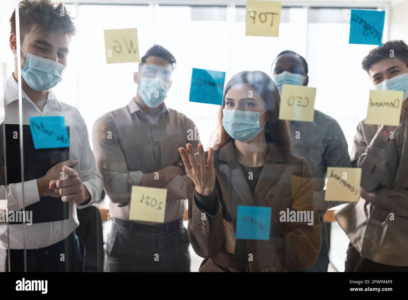 Businesspeople having meeting using sticky post-it notes on glass wall ...