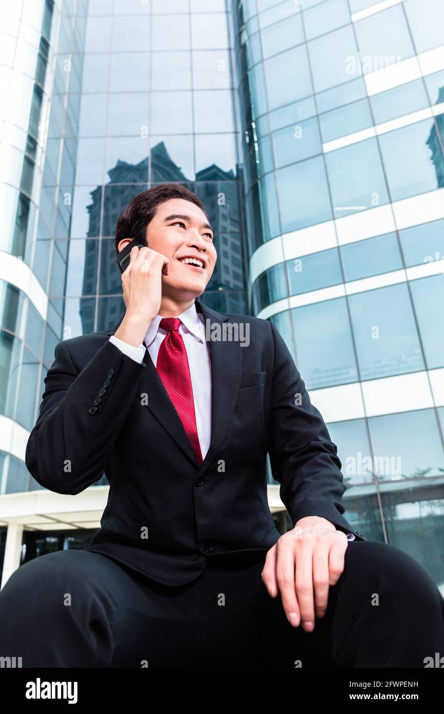 Asian businessman telephoning with smartphone in front of tower ...