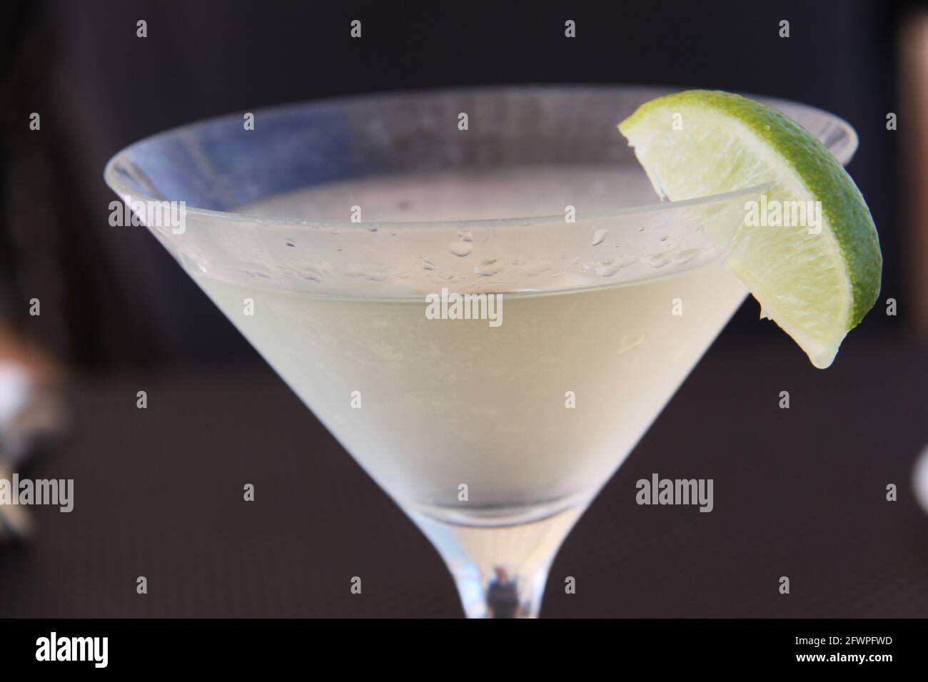 frosted cocktailglass with pale cocktail drink and lime wedge as ...