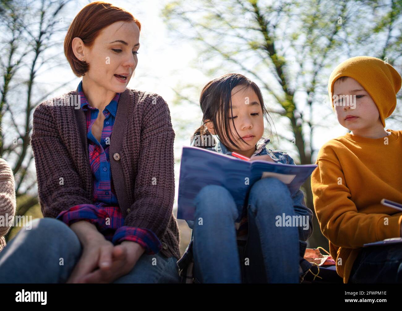 Teacher with small children sitting outdoors in city park, learning ...