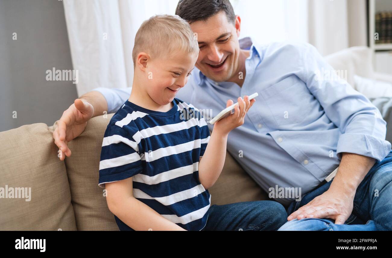 Father with happy down syndrome son indoors at home, using smartphone ...