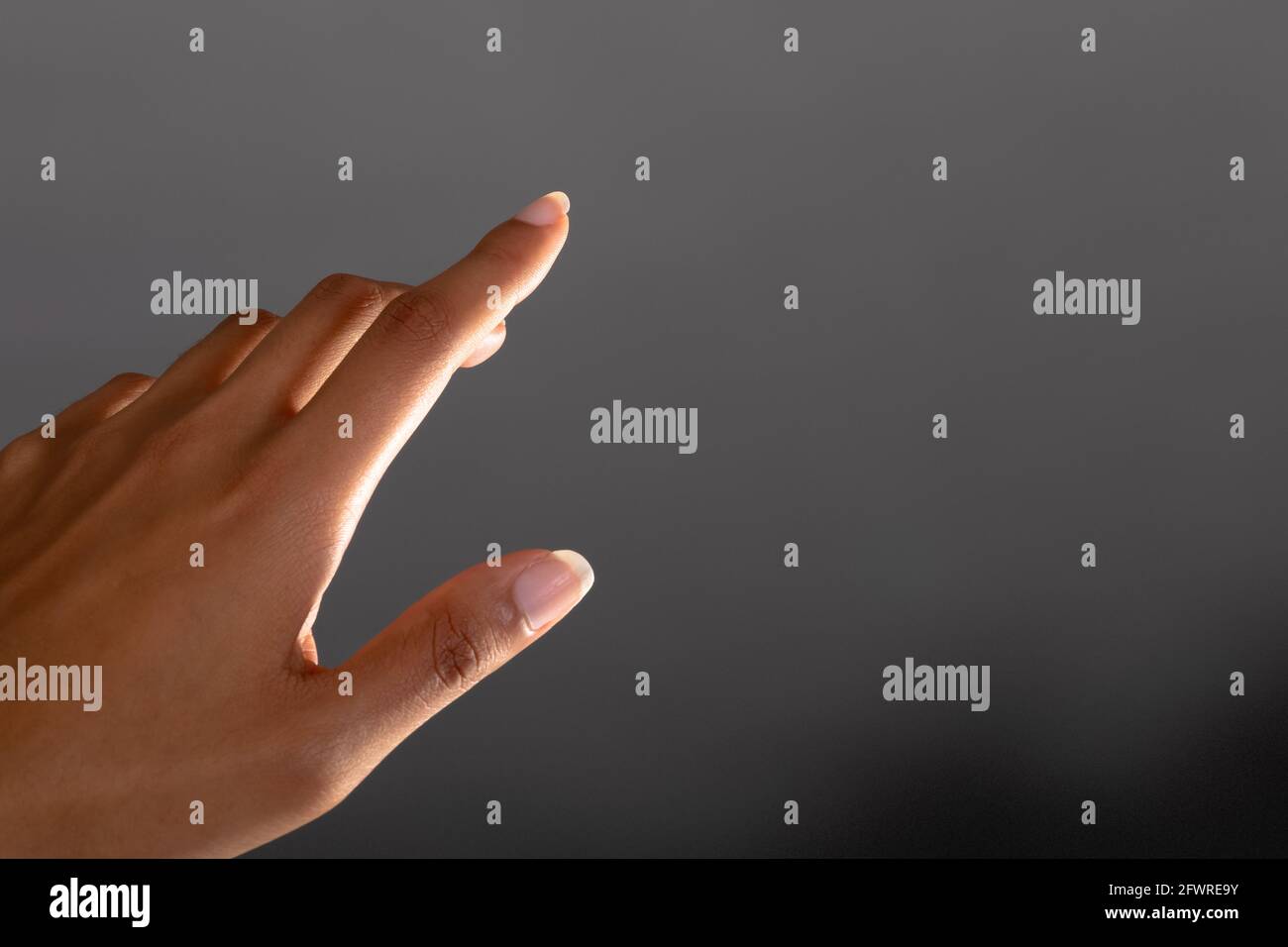 Close up of hand touching invisible screen against grey background ...