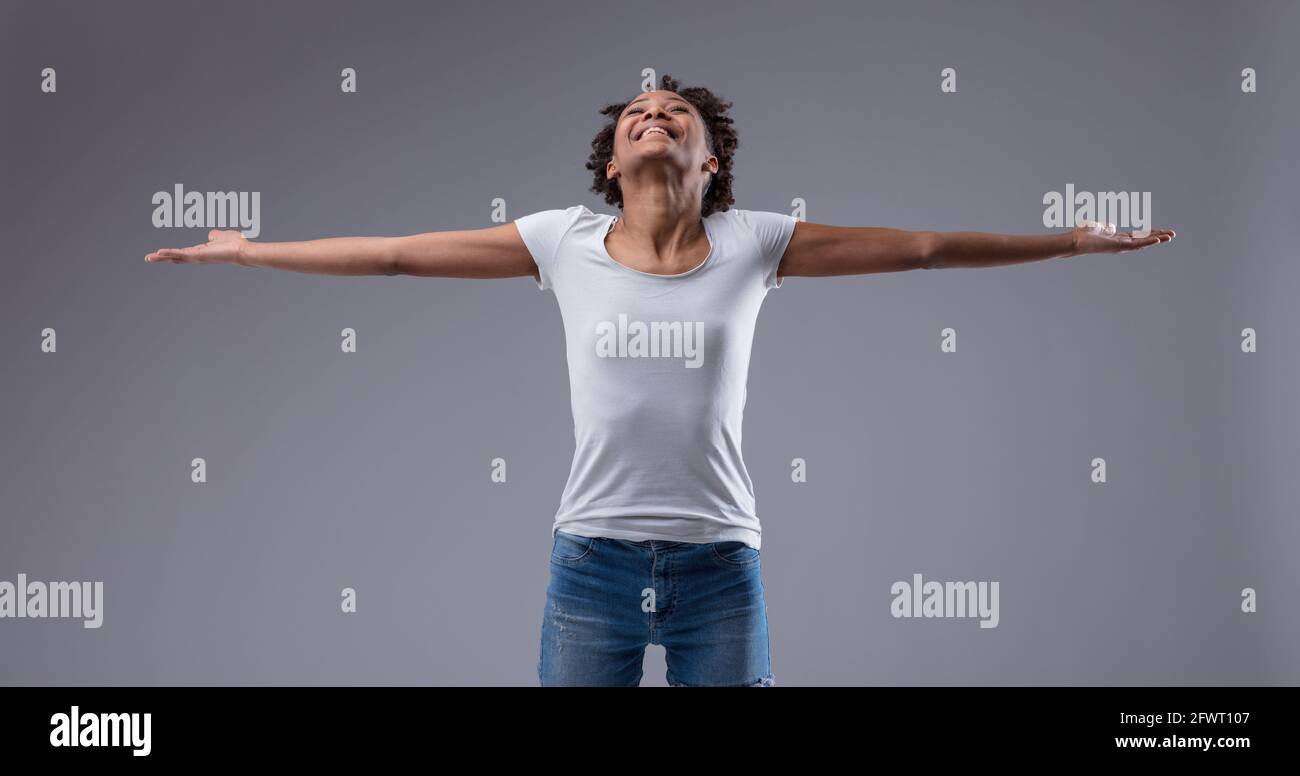 Gleeful exuberant young Black woman holding out her arms looking up ...
