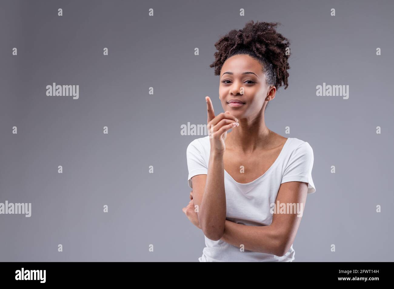 Smiling young woman raising a finger as she makes a point or identifies ...