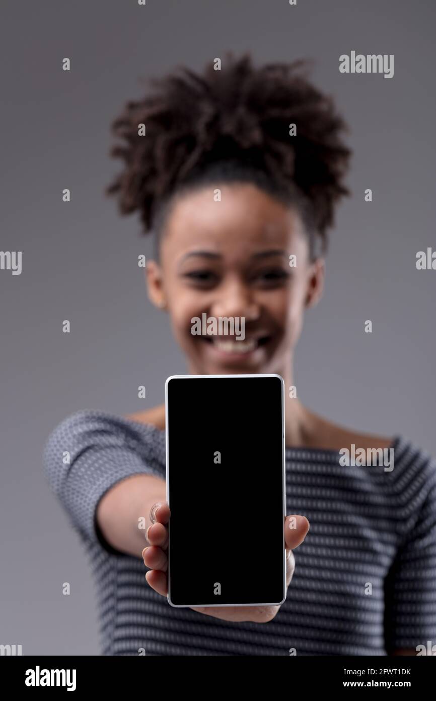 Happy young Black woman extending her blank mobile phone to the camera ...