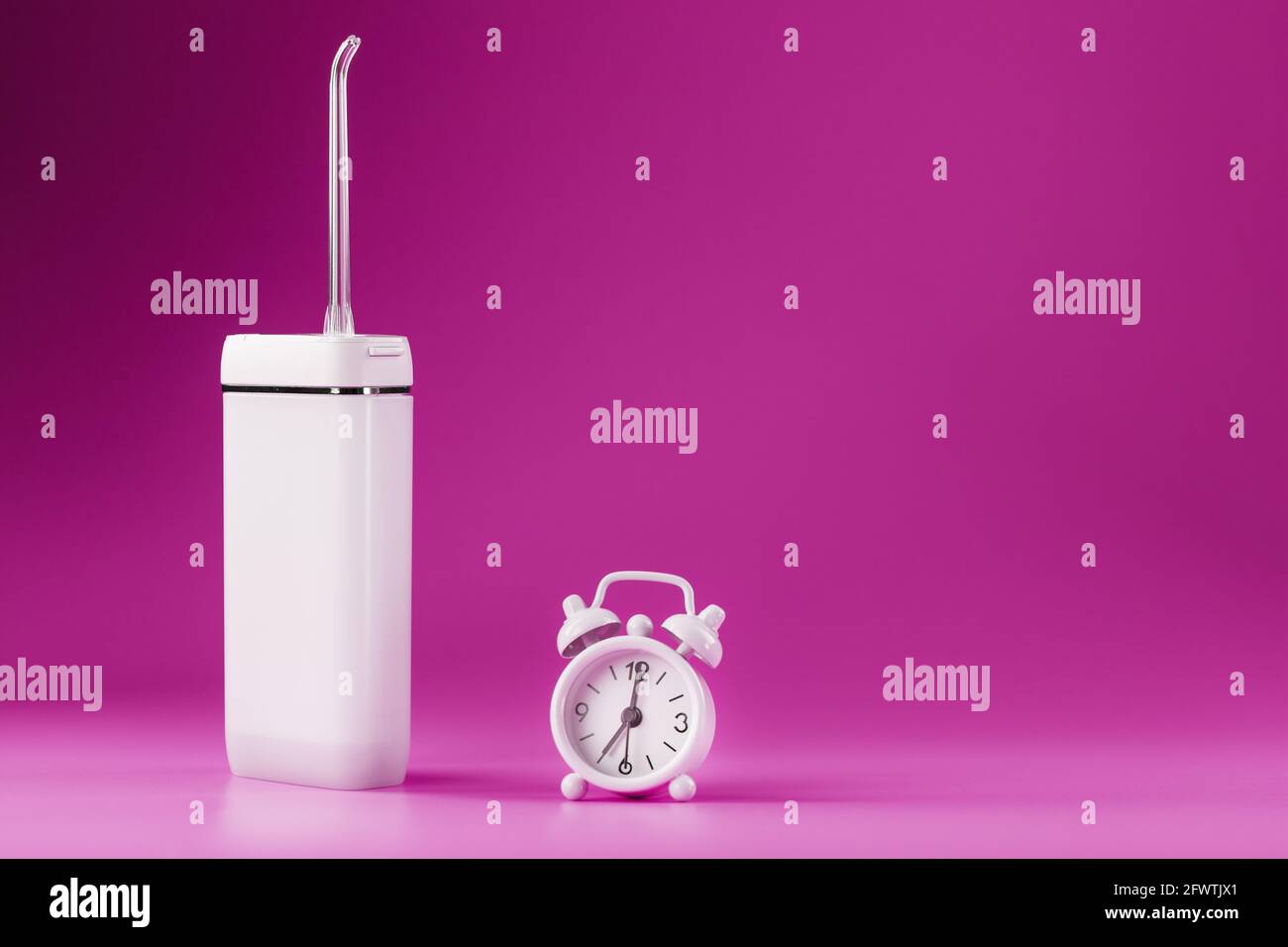 An irrigator for brushing teeth on a pink background with a clock. Oral ...