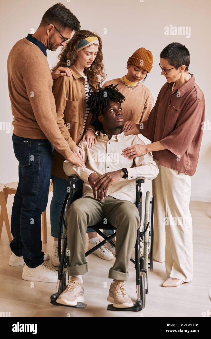 Vertical portrait of people comforting young man in wheelchair during ...