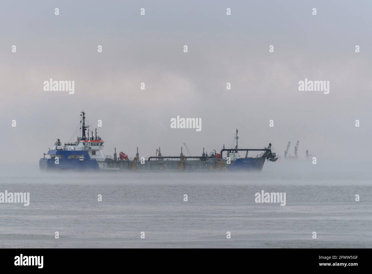 Vessel engaged in dredging at sunset time. Hopper dredger working at ...