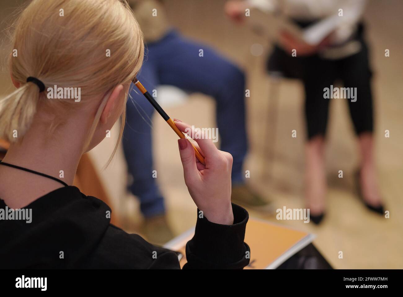 Young pensive blond female holding pen by temple during session Stock ...