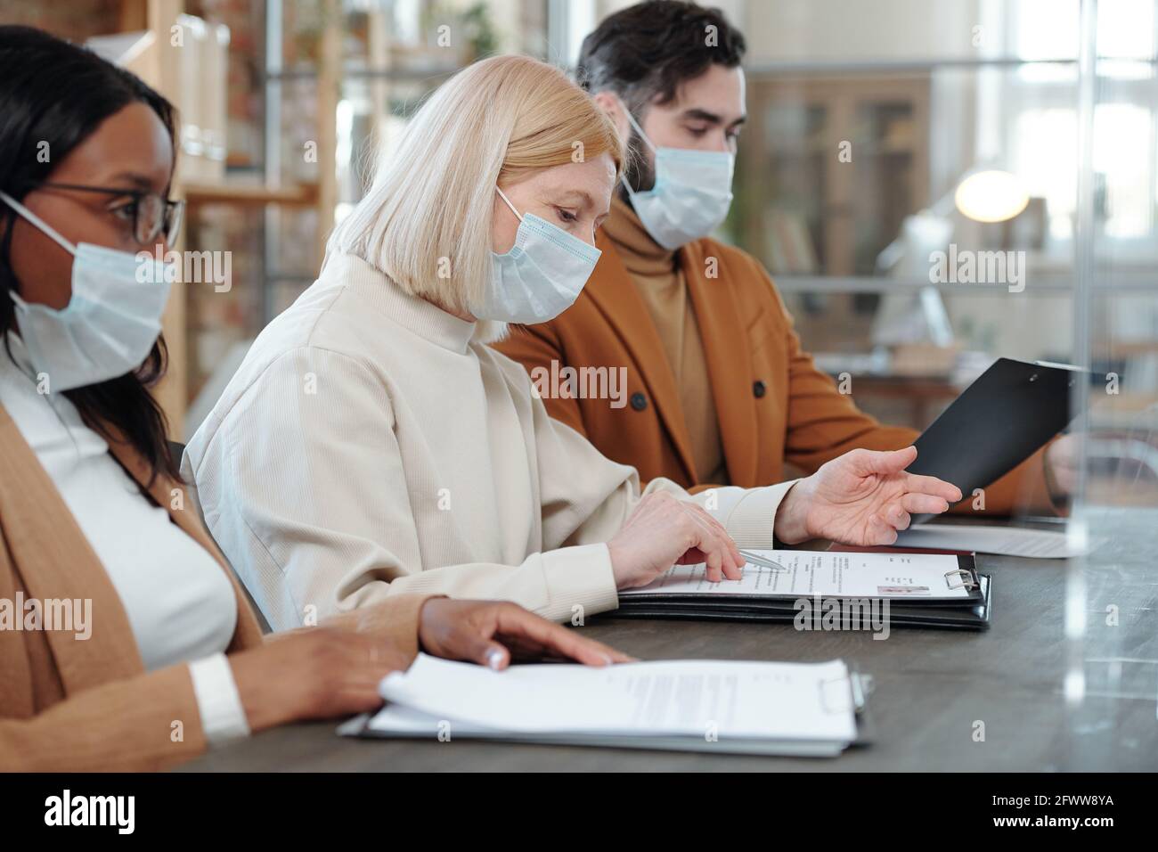 Team of serious strict multi-ethnic HR specialists in masks sitting at ...