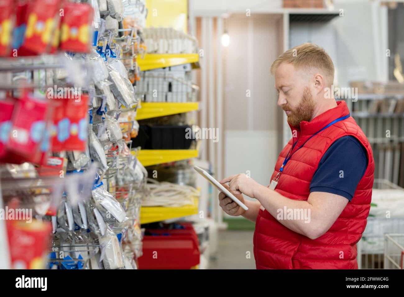 Young shop assistant in red uniform using tablet during work in ...