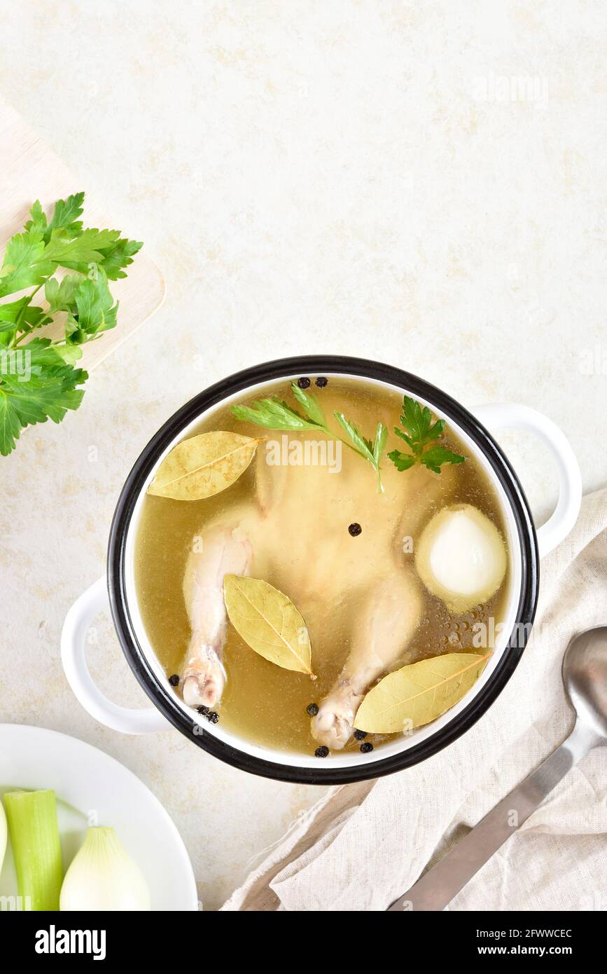 Chicken broth with vegetables and spices on light stone background with ...
