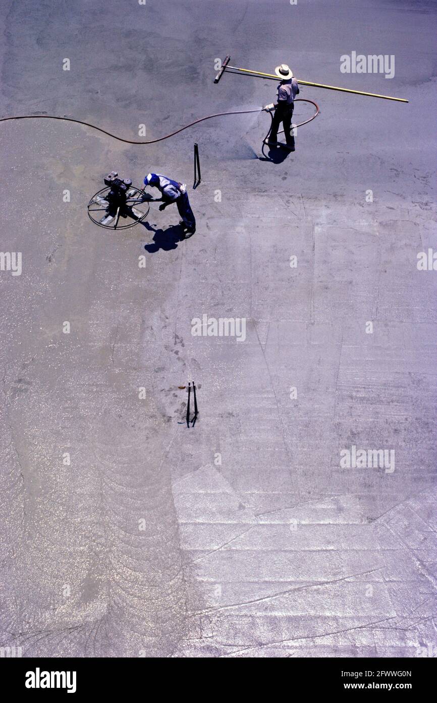Workers finish a concrete slab; floating; troweling and wetting the ...