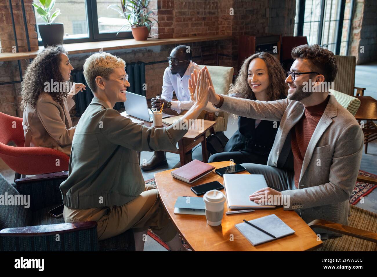 Successful colleagues giving each other high five over table in office ...