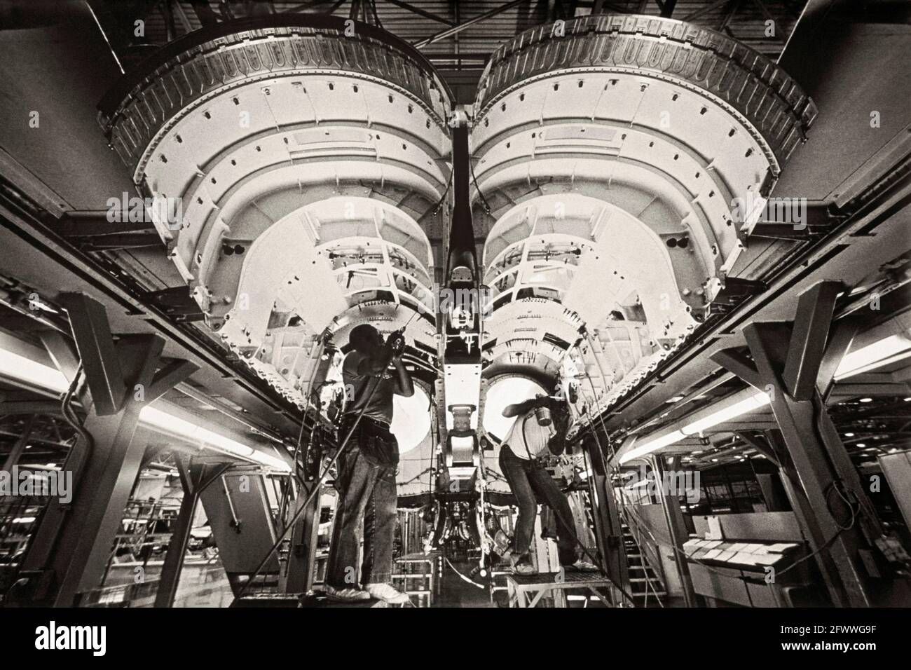 Beneath an FA-18 fighter aircraft on an assembly line; a Northrop ...