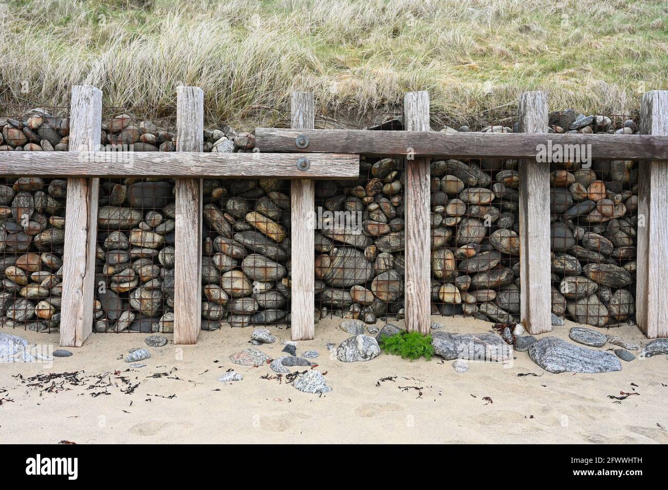 Coastal retaining wall of stone, metal mesh and wooden pillars. Sand in ...