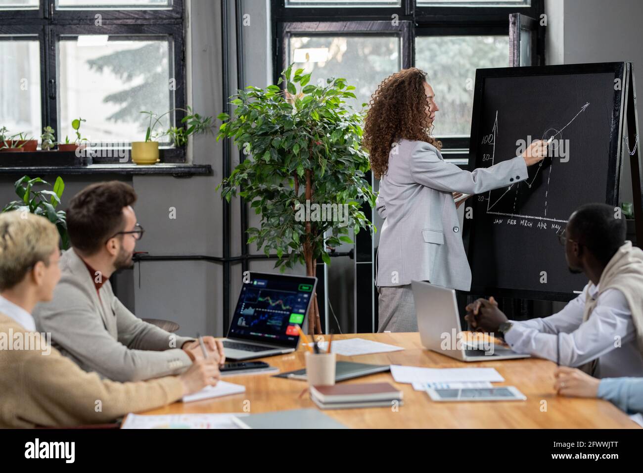 Elegant coach pointing at blackboard while making presentation of ...