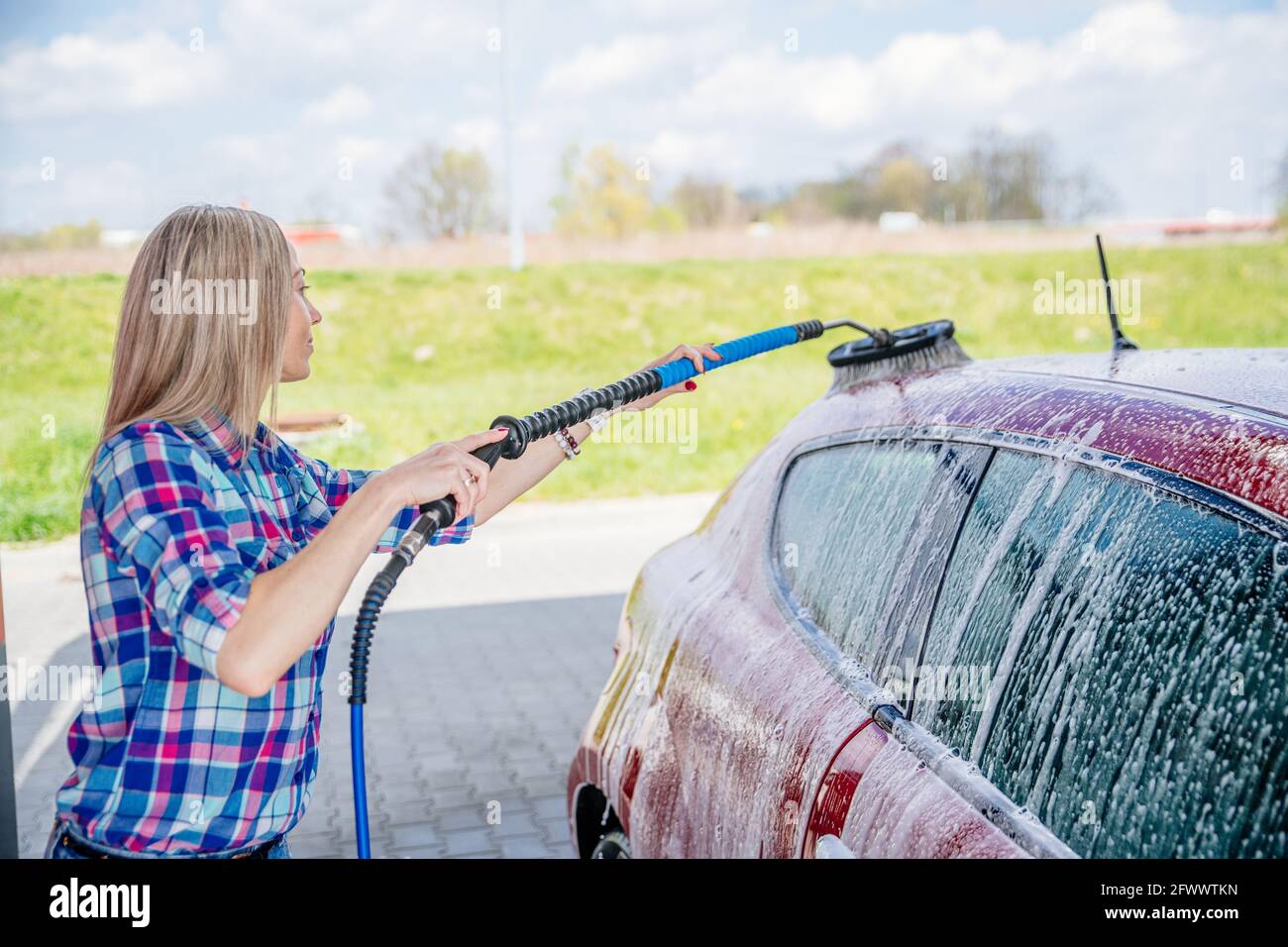 Woman in a plaid shirt washing the car in the station self-service car ...