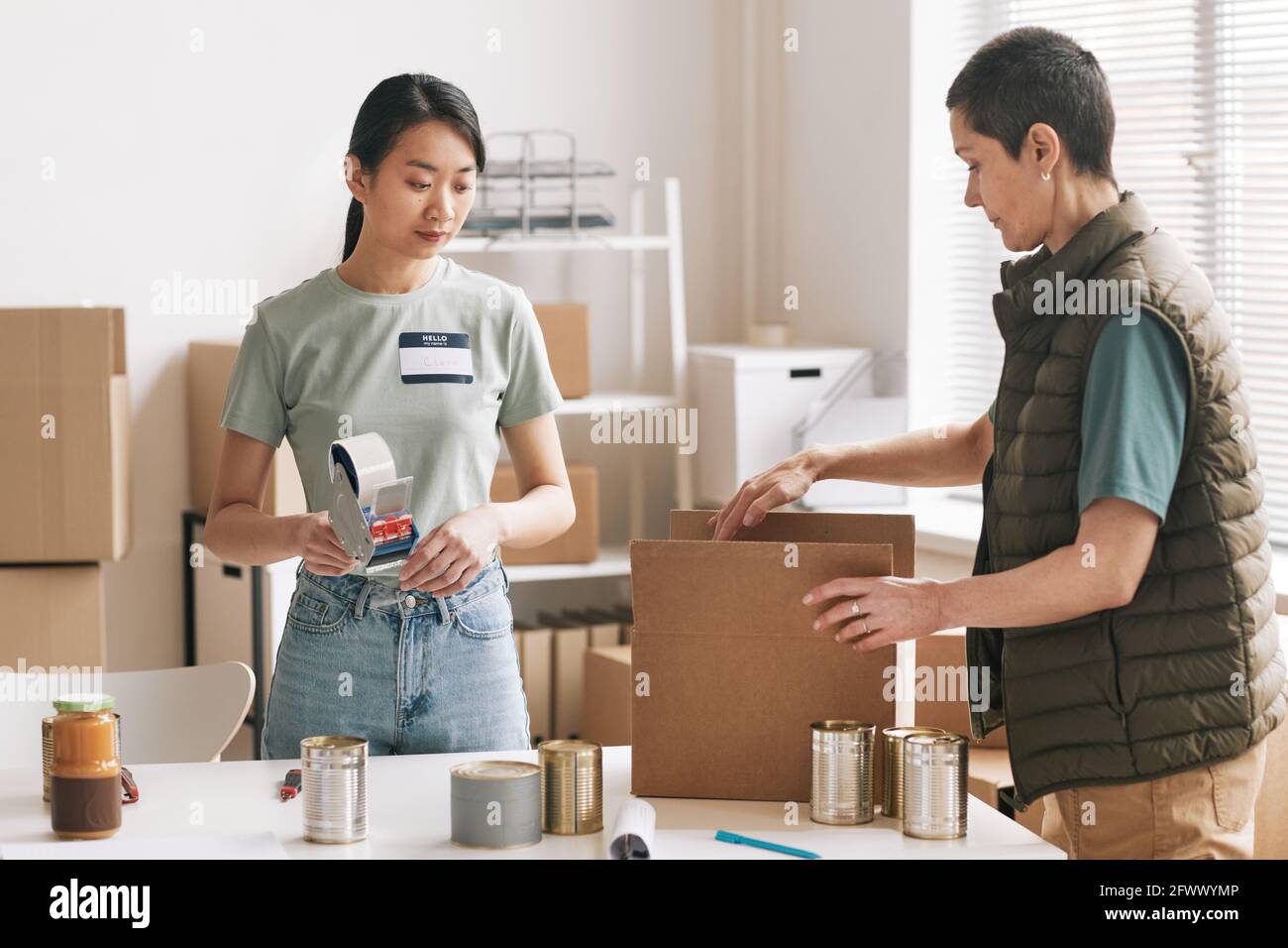 Portrait of two women packing boxes while volunteering at charity and ...
