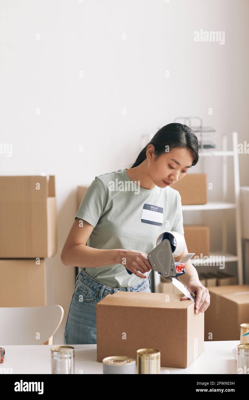 Vertical portrait of young woman packing boxes at charity and donations ...