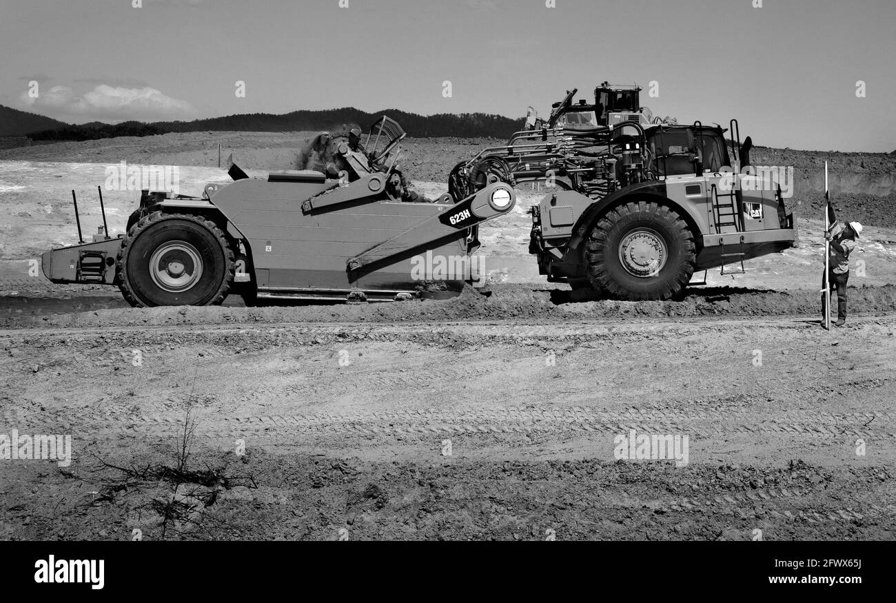 Road construction workers use a Caterpillar wheel-tractor scraper to ...