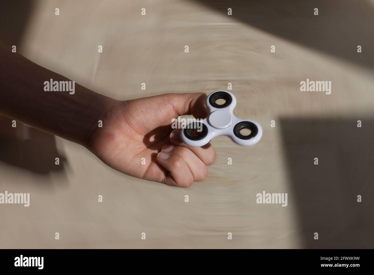 Closeup of a hand holding a fidget spinner on a blurry floor background ...