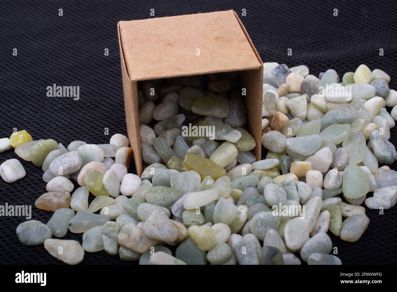 Stone pebbles gravels around brown cardboard box on a black background ...