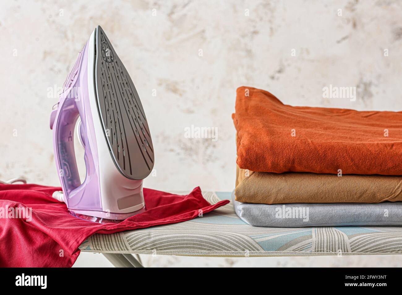 Electric iron and clean clothes on light background Stock Photo - Alamy