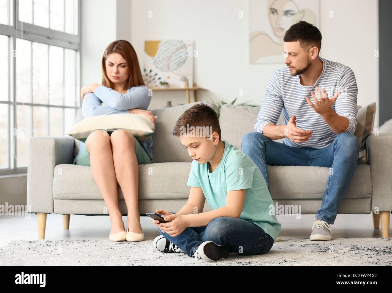 Little boy using mobile phone and his sad parents at home Stock Photo ...