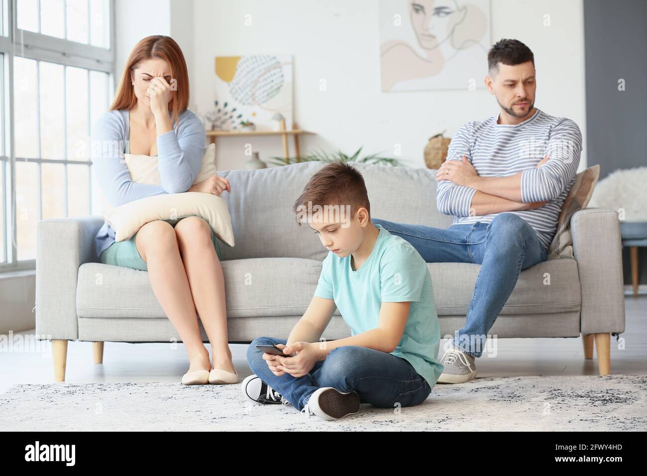 Little boy using mobile phone and his sad parents after quarrel at home ...