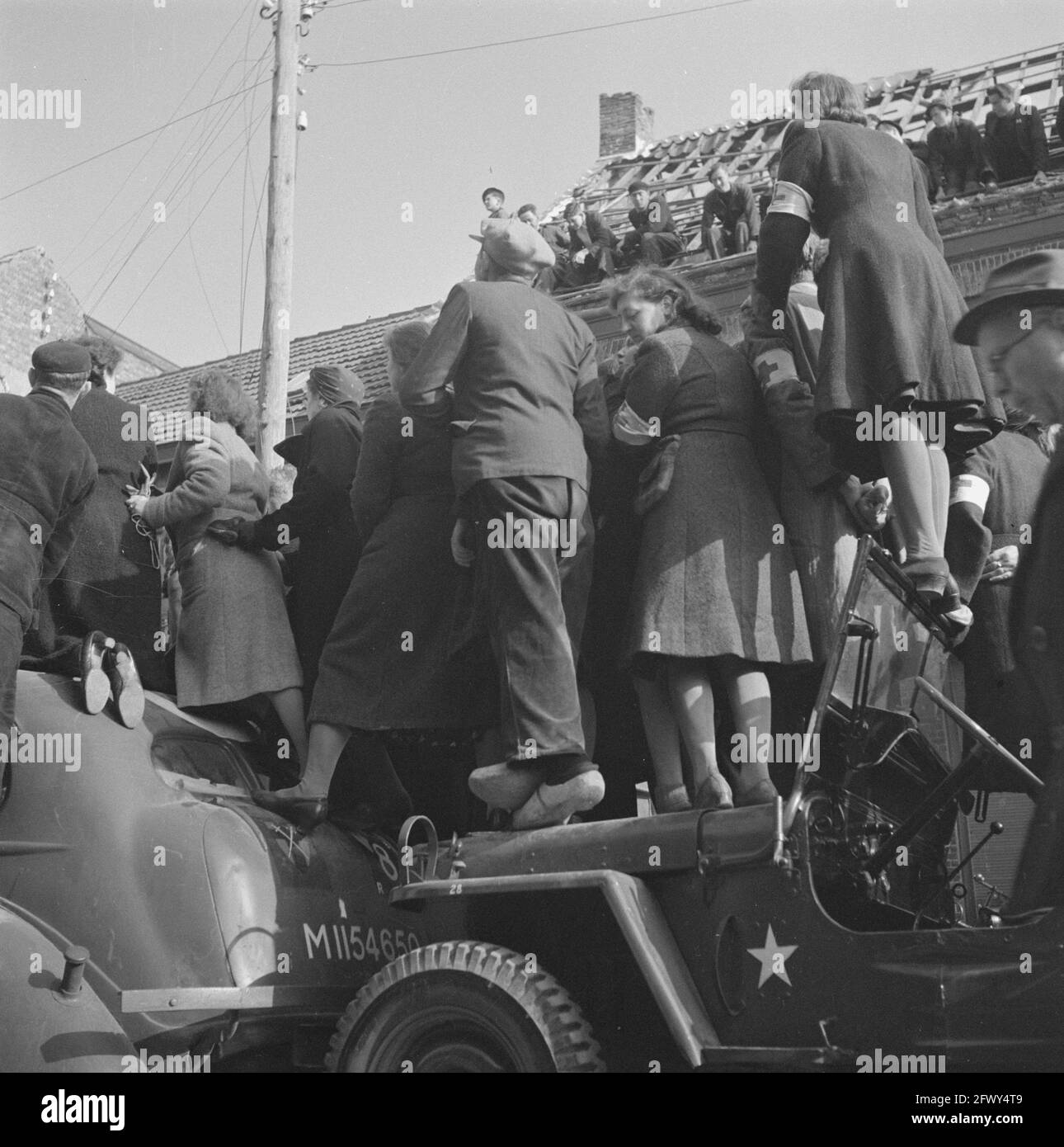 Crowd standing on top of jeeps and cars or on roofs of houses to catch ...