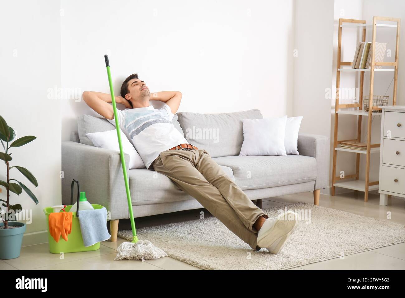 Young man with cleaning supplies relaxing in living room Stock Photo ...