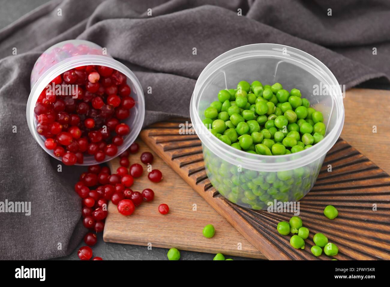 Plastic containers with green peas and cranberry on dark background ...
