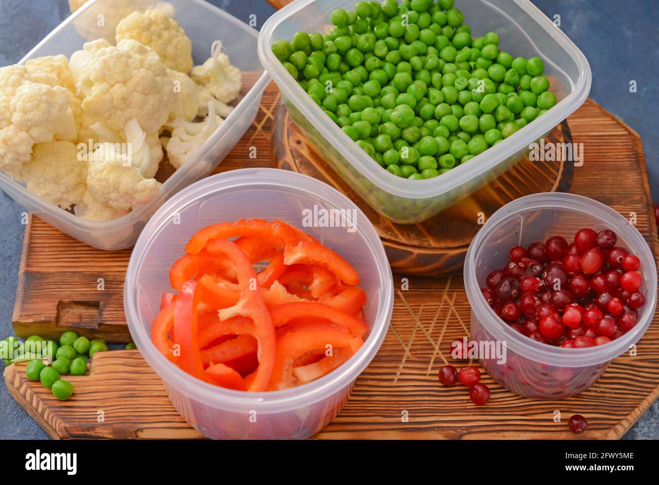 Plastic containers with vegetables and cranberry on color background ...
