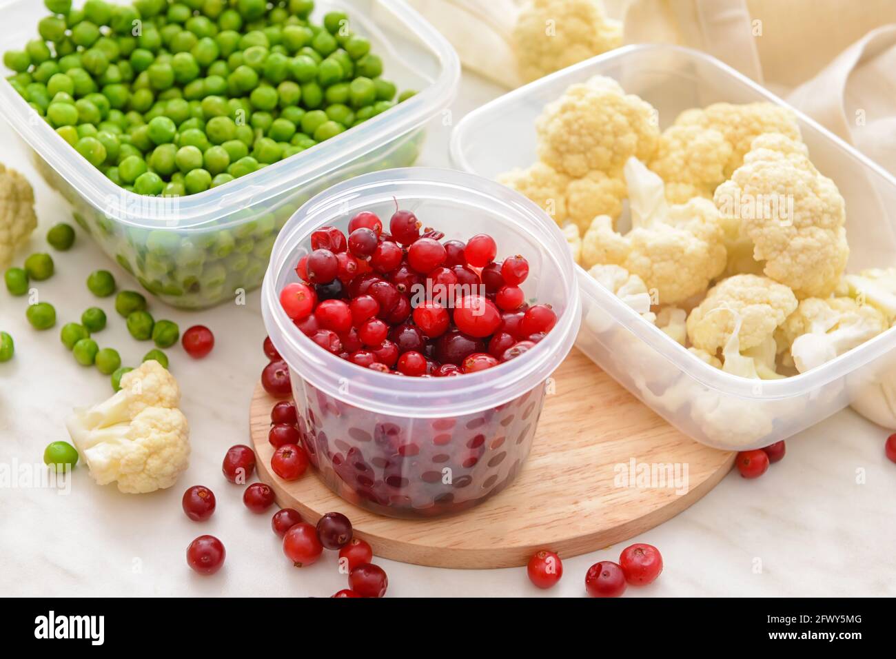 Plastic containers with vegetables and cranberry on light background ...