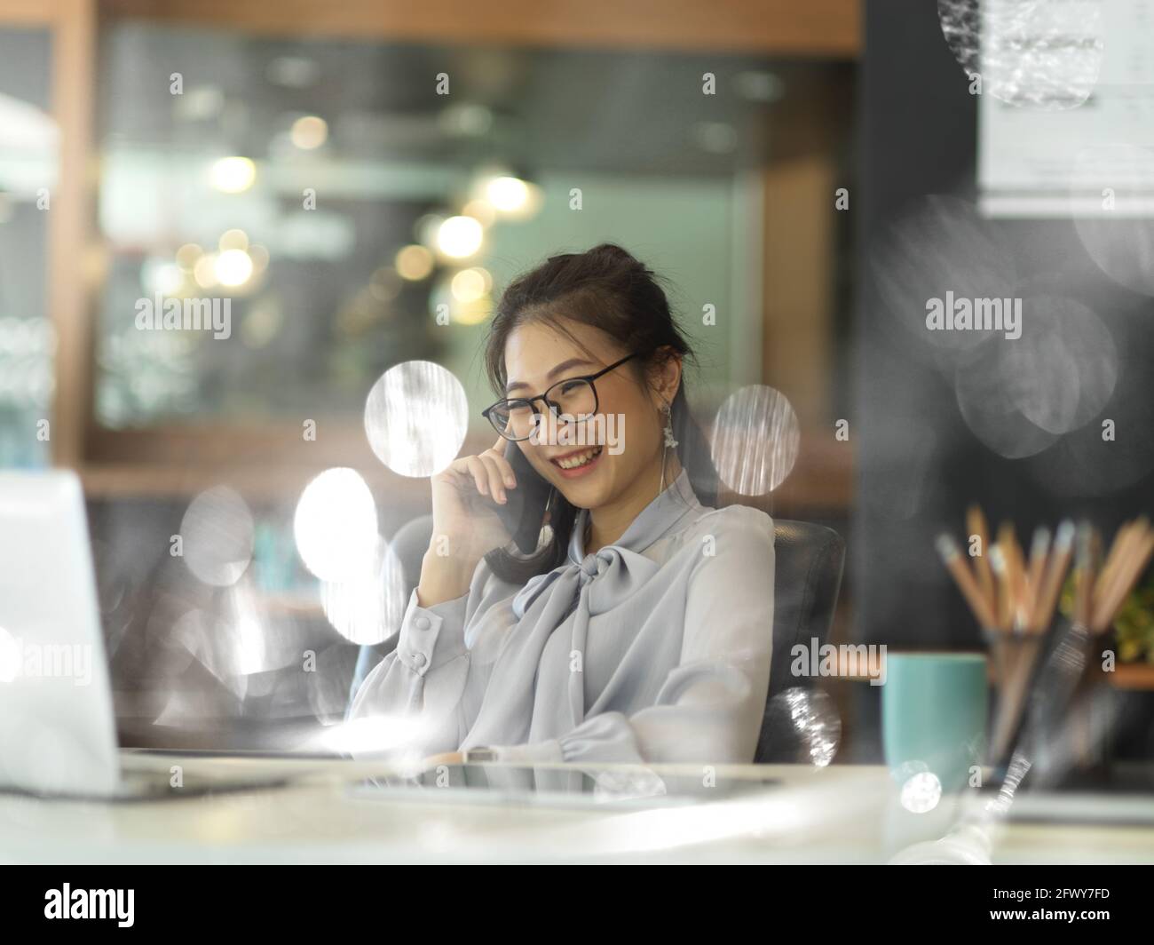 View through glass window of businesswoman talking on the phone in ...
