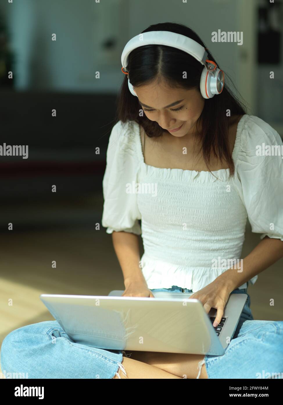 Portrait of female with headphone using laptop on her lap while crossed ...