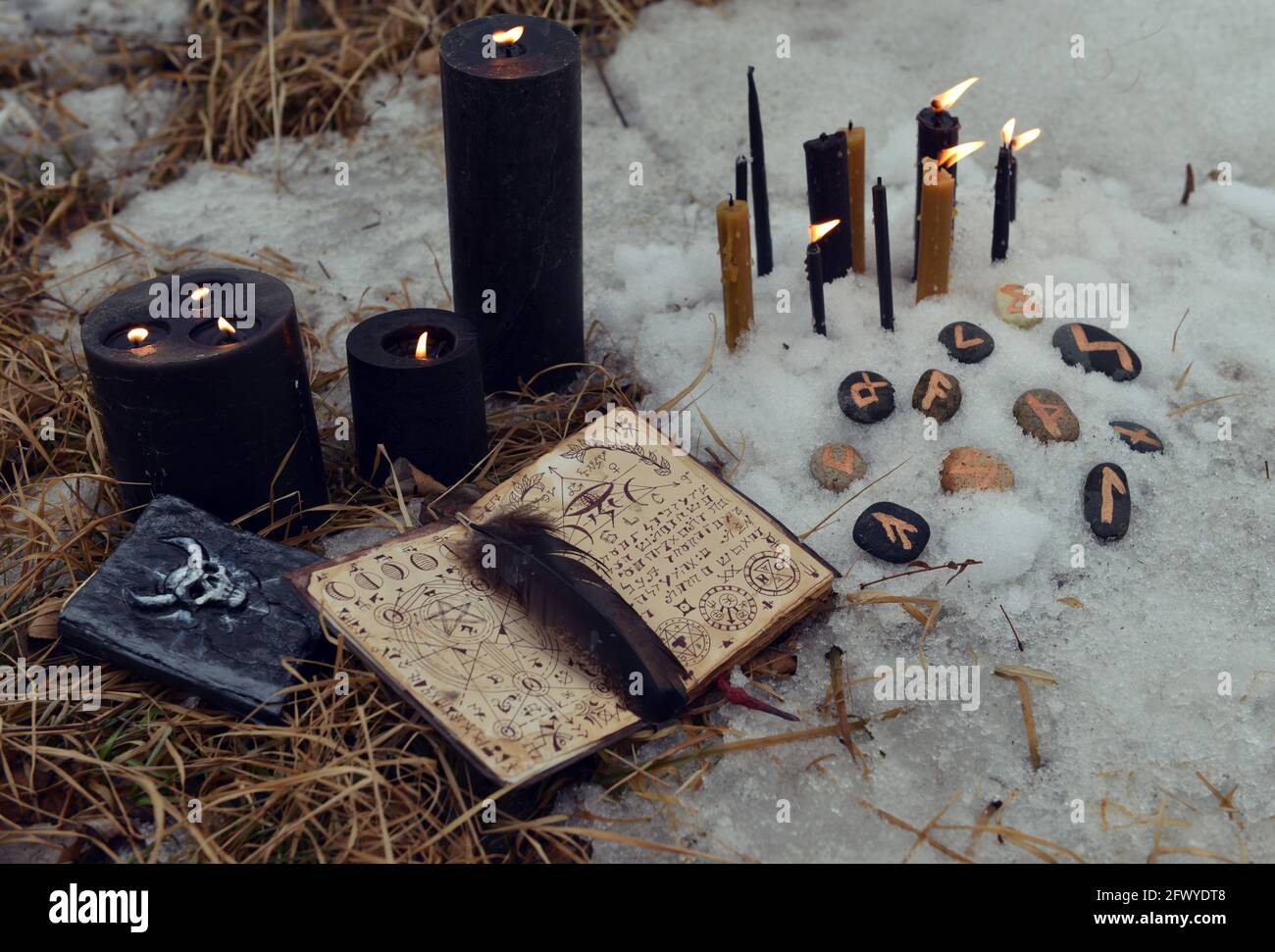 Magic book of spells, black candles and runes in snow outside. Esoteric ...