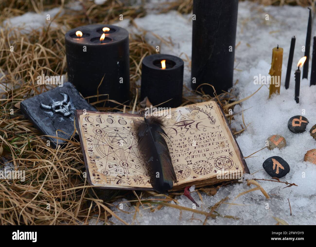 Open book of spell with black candles and runes in snow. Esoteric ...