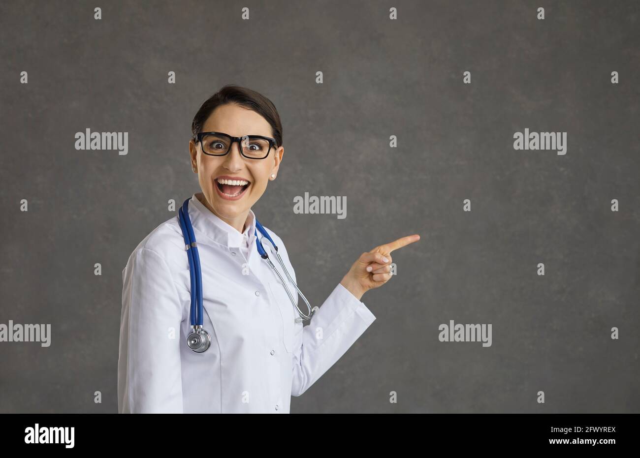 Funny crazy female doctor standing on gray background smiling with wide ...